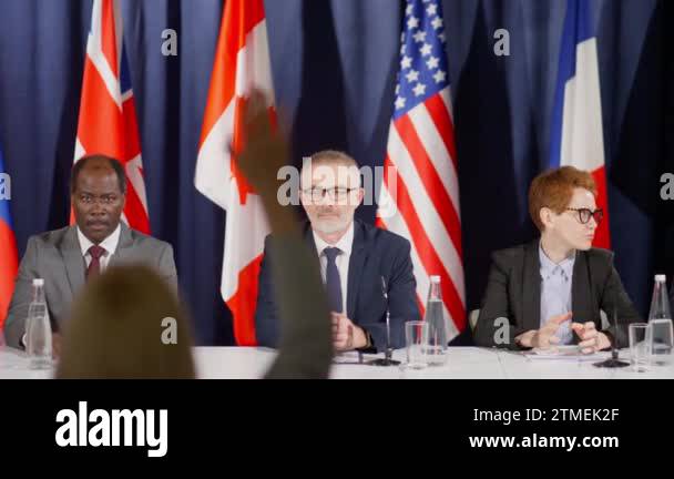 Panning shot of world political leaders sitting by national flags of ...