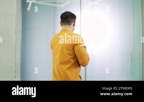 Rear view. A man in a shirt opens a glass door in a modern building and ...