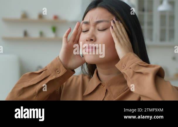 Tired sick Asian woman feel headache pain massaging temples touch aching head hurt grimace ...