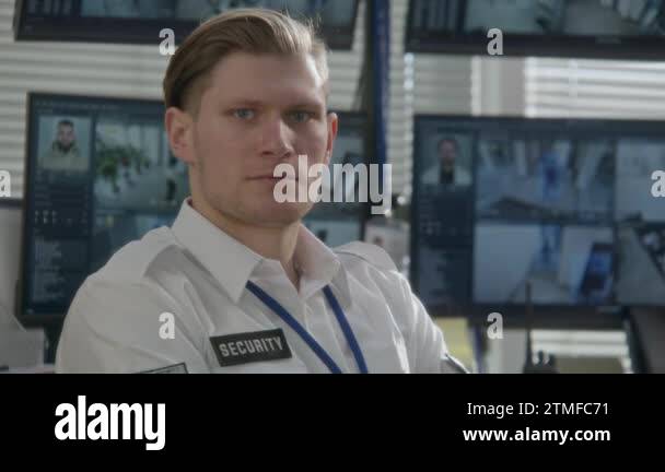 Security worker in uniform sits in observation room and looks at camera ...