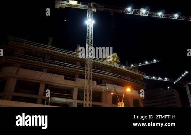 Illuminated tower crane at a high-rise building construction site. High ...