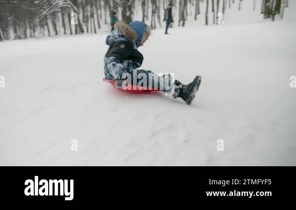 Young boy laughing and smiling while sledding down a snowy hill and ...