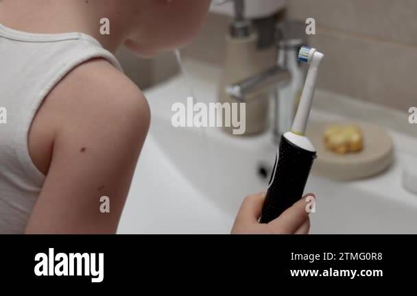 kid boy washing teeth with electric in bathroom looking in mirror and ...