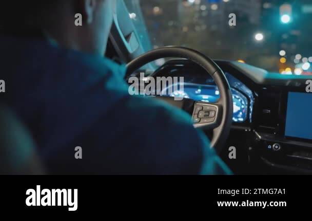 Man driving car through the streets of night city. Glare in the window ...