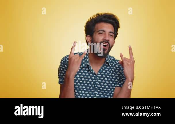 Overjoyed young indian man showing rock n roll gesture by hands, cool ...