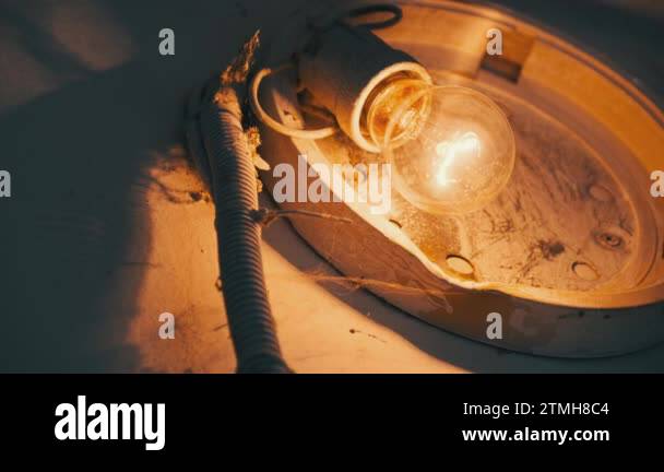 An incandescent light bulb glows in an old broken lamp on the concrete ...