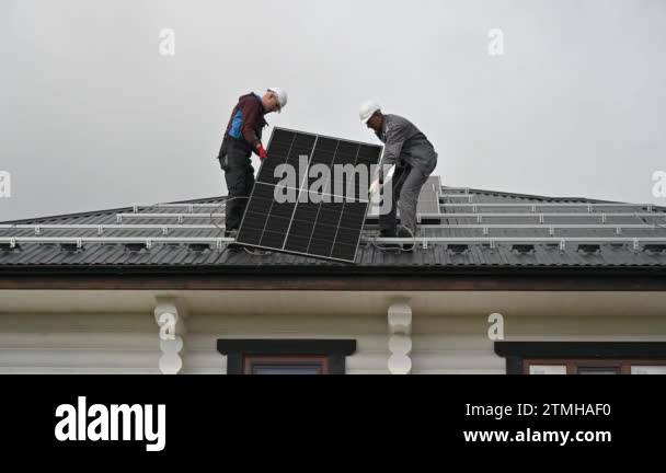 Men workers installing solar panel system on roof of house ...