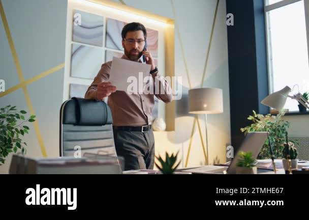 Bearded boss speaking telephone standing modern office leaning on chair ...