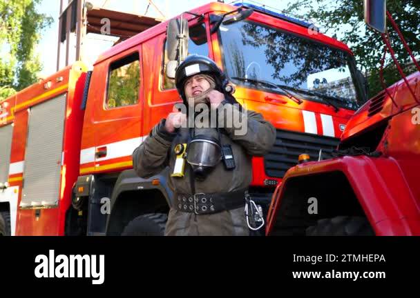 Young fireman taking off helmet and balaclava stands near fire engine ...