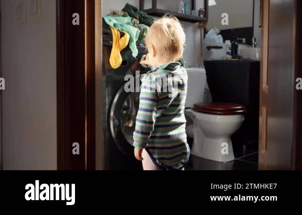 Little baby boy pressing knobs and buttons on working washing machine ...