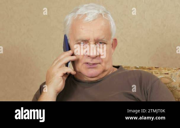 The man at the age of talking on a cell phone at home on the couch. His ...