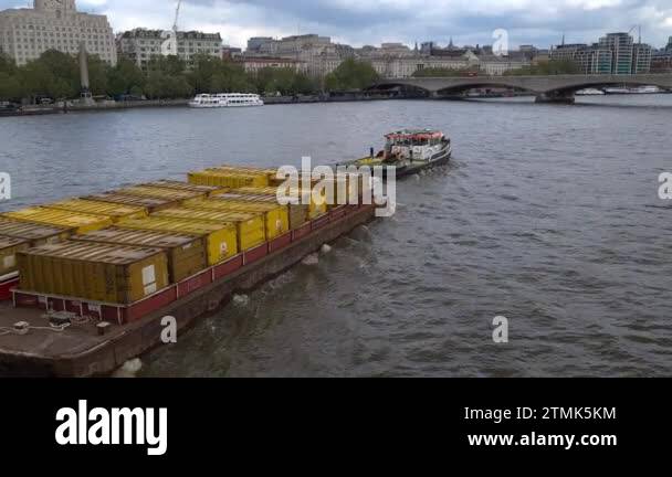 London. UK- 05.17.2023. A tug boat pulling barges full of shipping ...