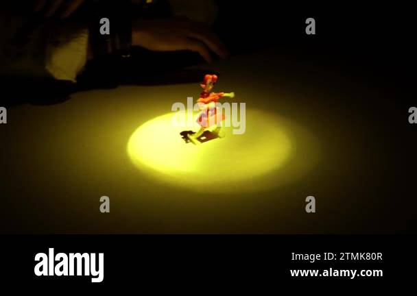 A mans hands place a mechanical puppet on a table illuminated by a beam ...
