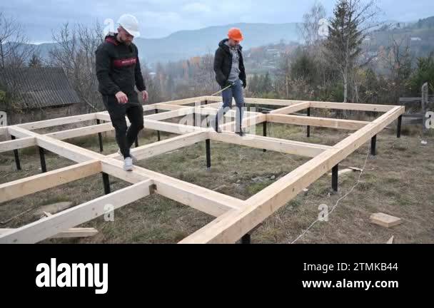 Men workers building wooden frame house on pile foundation. Carpenters ...