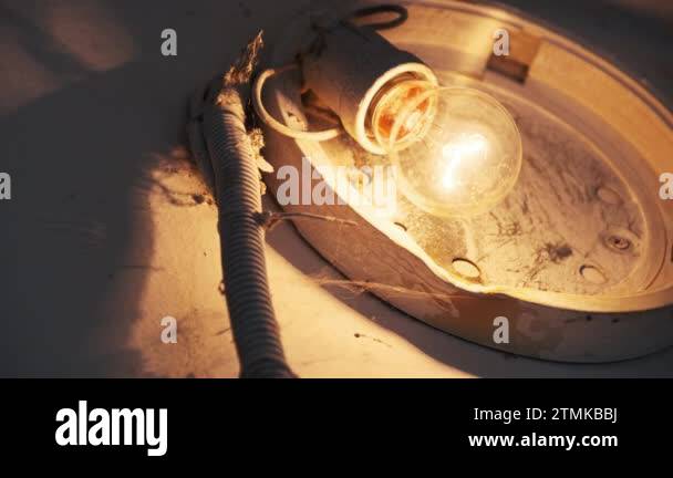 An incandescent light bulb glows in an old broken lamp on the concrete ...