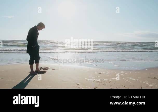 A side view of a young man standing barefoot on a beautiful sandy beach ...