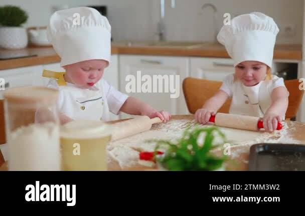 Adorable 3 years old boy and girl in chef hats and aprons rolling out ...
