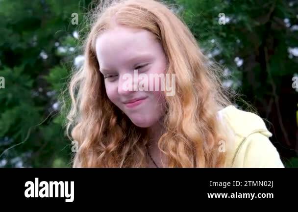 red-haired teenager girl against background of trees to be embarrassed ...