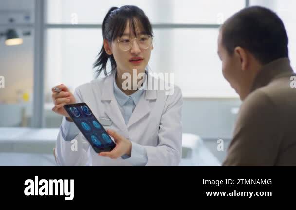 Asian female doctor showing CT scan image on digital tablet to male ...