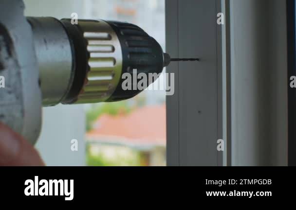 Male uses electric drill to drill holes in plastic window frame to ...