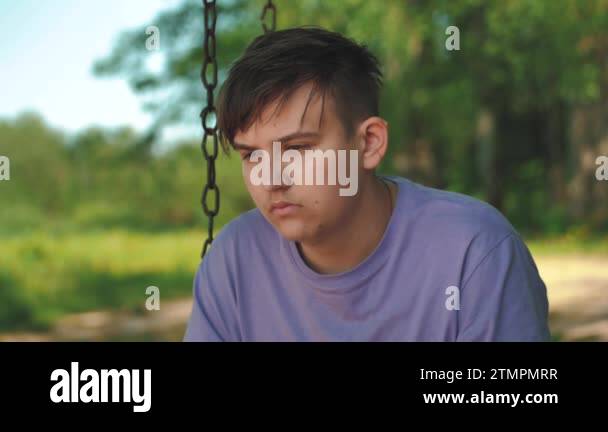 Guy is sitting on the swing in a depressed state. Close-up face of sad ...