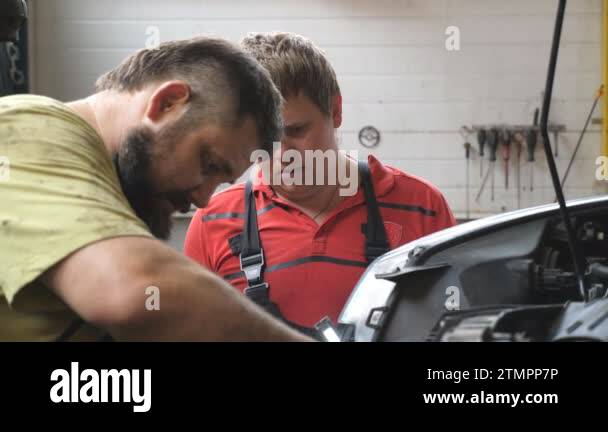 Profile of two mechanics works with car at garage. Portraits of ...