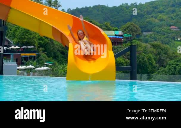 Woman in swimwear slides down a water slide in a swimming pool. Girl ...