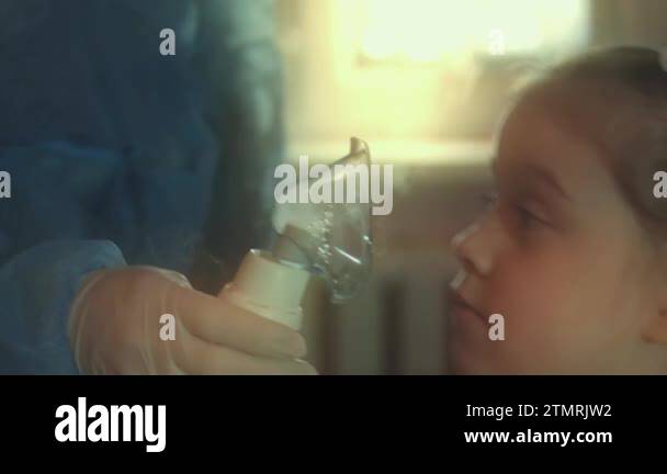 Beautiful little girl makes inhalation using a compressor inhaler while ...