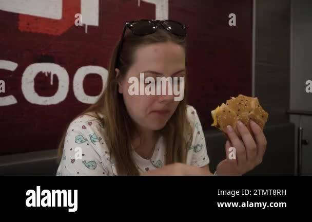 Young hungry woman greedily eating a meat burger in a fast food ...