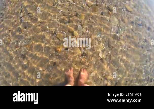 Woman standing bare feet barefoot on sandy rocky seabed with clear transparent water with waves ...