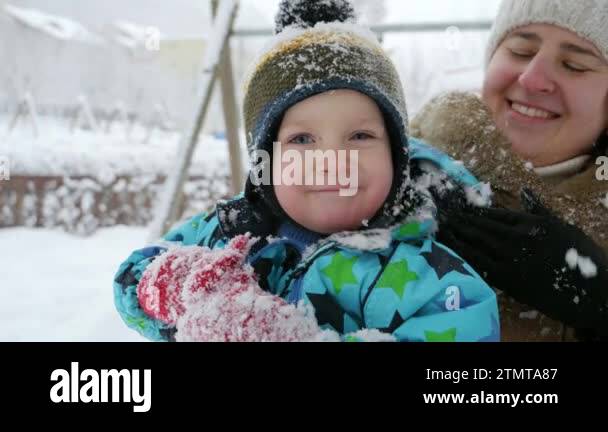 Young caring mother shaking off snow from her baby son after playing in ...