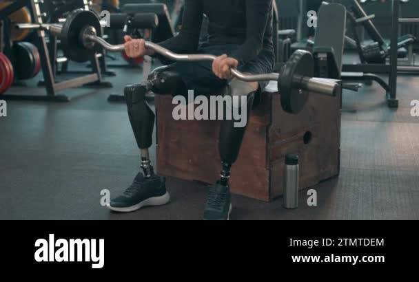 serious disabled man sitting on fitness box holding barbell in hands ...