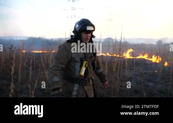 Young fireman in uniform going on burnt grass at countryside. Male ...