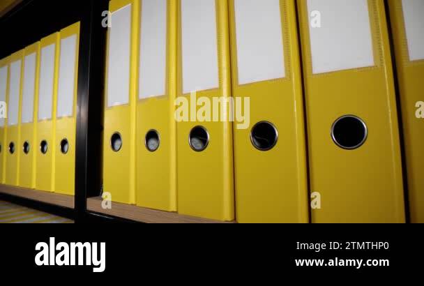 Yellow folders put in long line on shelf of rack in office premises ...