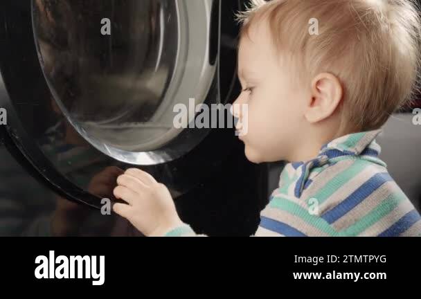 Portrait of baby boy watching washing machine spinning its drum. Doing ...