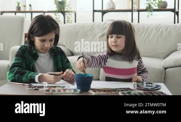 Caucasian brother and sister are seated on the floor near a table ...