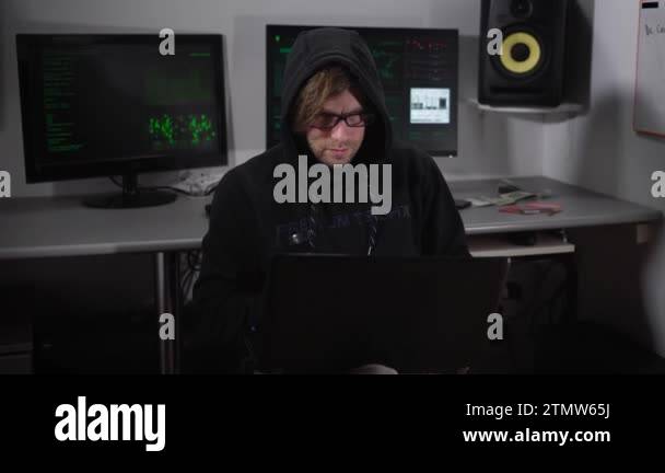 Young hacker in black working on laptop sitting alone in the room with ...