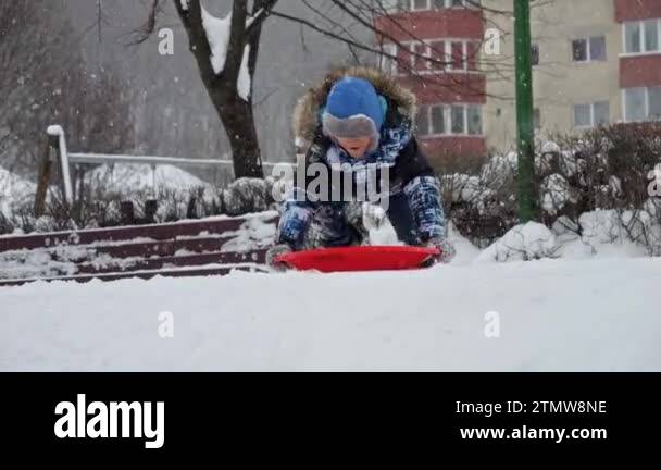Young boy with a big smile as he slides down a snowy slope on his ...