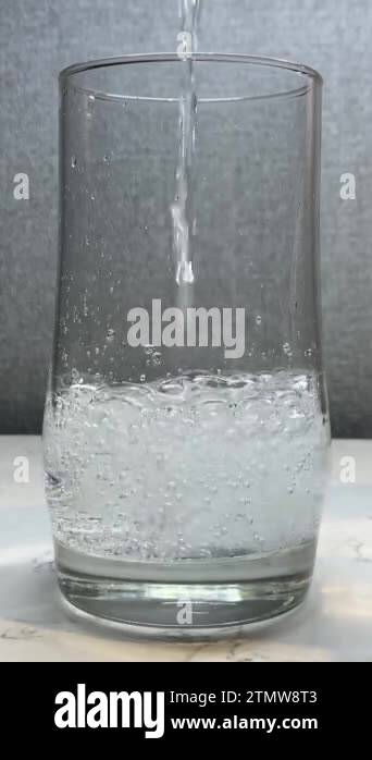 pouring water into a glass real time close-up bubbles rise up. soda is poured into a transparent ...