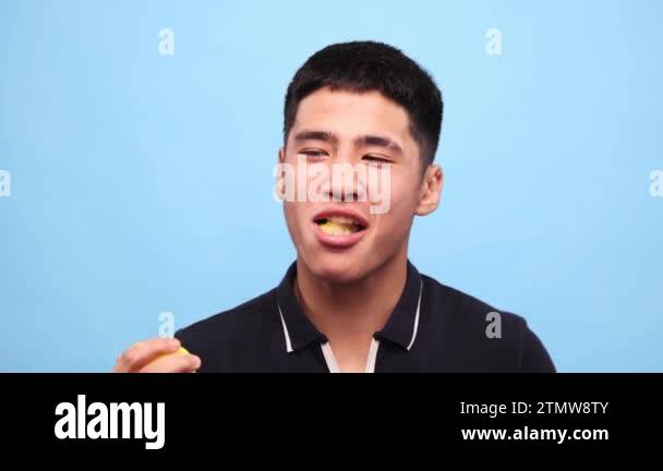 Young asian guy biting lemon against blue studio background. Handsome ...