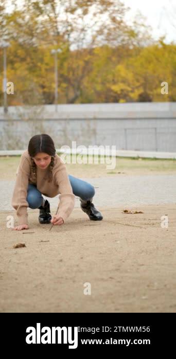 Girl with two braids drawing hopscotch in the sand with a stick ...