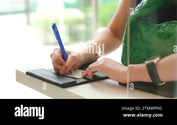 A woman signs a bill at a checkout counter after shopping. She looks at ...