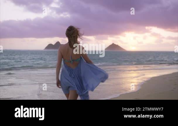 Back view of woman walking by ocean beach at sunrise relaxing on summer ...