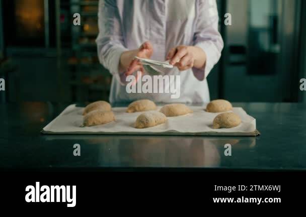 concentrated beautiful woman baker sprinkles flour through sieve raw bread fresh dough before ...
