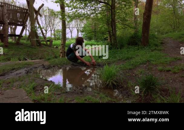 Boy plays in a wet mud puddle in nature playground in park on sunny ...