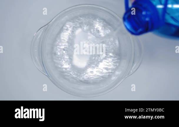Water is poured into a glass bowl on a white background. Isolated. The ...
