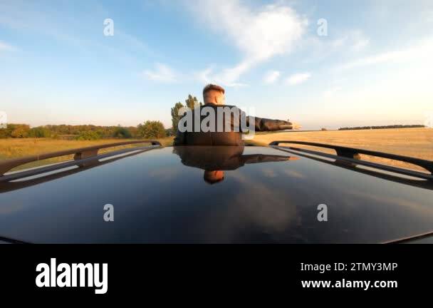 Young guy standing out of car sunroof and playing with wind while ...