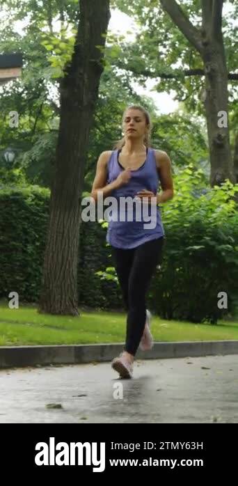Vertical Screen: Slow motion woman in sportswear running in park on wet ...