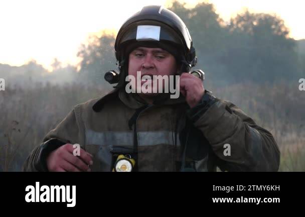 Young fireguard in uniform taking off helmet on countryside at the ...