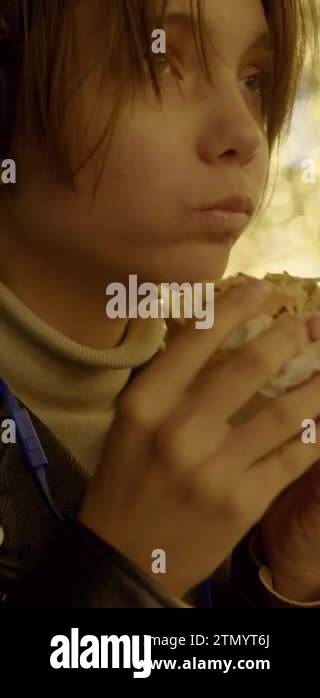 Vertical footage of a teenage girl eating hamburger on the street at ...